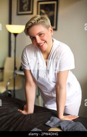 Professional masseuse in white uniform performs relaxing leg massage on ...