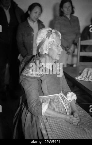 Visitors and a female actor in period colonial clothing stand outside ...