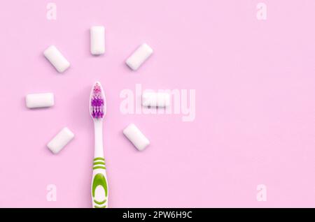 Toothbrush and chewing gums lie on a pastel pink background. Top view ...