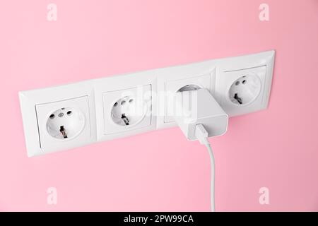 Charger adapter plugged into power sockets on pink wall. Electrical ...