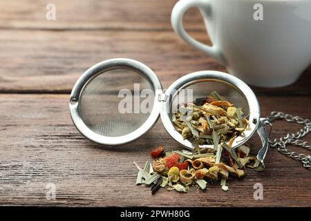 Snap infuser with dried herbal tea leaves on white wooden table, top ...