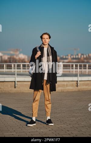 Young man in old wool coat, scarf and short trousers outdoor with hand ...