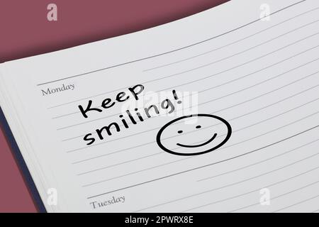 A Keep smiling diary reminder message open on desk Stock Photo - Alamy