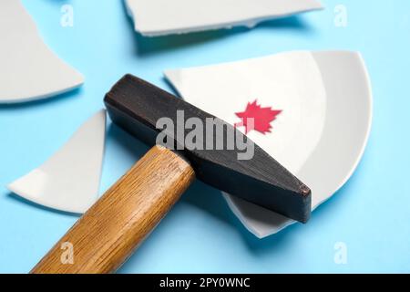 Hammer and broken plate with paper maple leaf on blue background ...