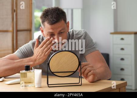 Sleep deprived man covering up dark circles with concealer near mirror ...