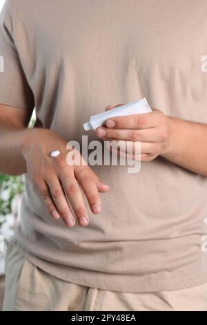 Man applying ointment from tube onto his hand on light blue background ...