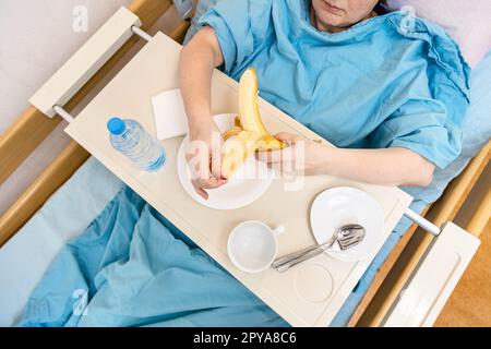 top view of sick woman peeling banana in homecare hospital bed at home ...