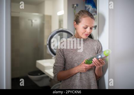 Young blonde woman doing laundry sitting by washing machine suffering ...
