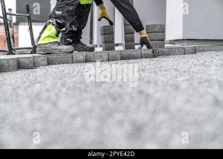 Worker laying interlocking pavers during sidewalk construction with ...