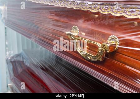 New wooden coffin with a handle made of yellow metal, packed in plastic ...