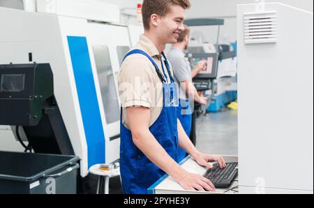 Worker using keyboard to enter data into a machine on factory floor ...