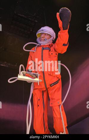 A Russian cosmonaut in an orange space suit floats above a capsule. A ...