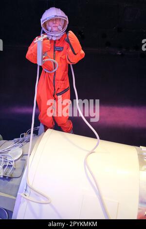A Russian cosmonaut in an orange space suit floats above a capsule. A ...