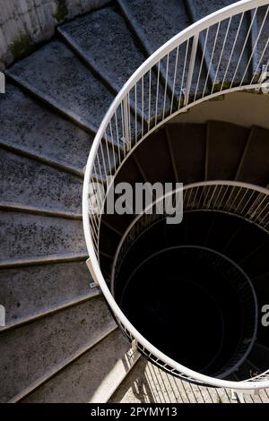 A concrete and metal spiral staircase descending down into a dark stair ...