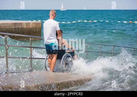 Woman with disability at beach goes to swimm on a wheelchair with ...