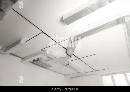 Conduits with cables and ventilation system on white ceiling, low angle ...