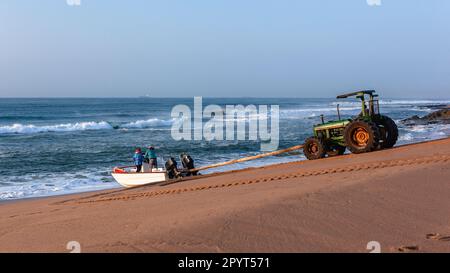 Fishing boat entry into surf ocean waves off beach sand by tractor ...