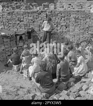 Undated photo of a group of children watching a puppet show among piles ...