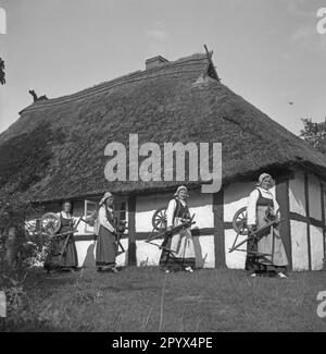 Women carry their spinning wheels through a village on the Baltic coast ...