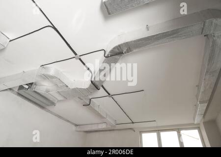 Conduits with cables and ventilation system on white ceiling, low angle ...
