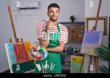 Brazilian young man holding painter palette at artist studio skeptic ...