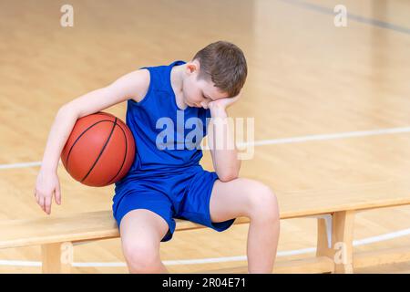 Sad disappointed boy with basketball ball in a physical education ...