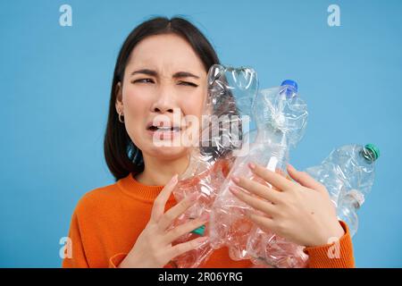 Crying asian girl holding plastic bottles, being upset, recycling ...