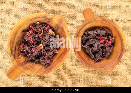 Dry fragrant karkade tea in two wooden cups on a jute cloth, macro, top ...