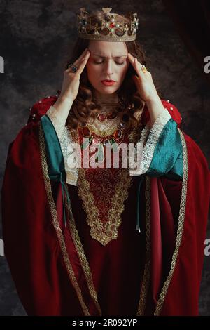 stressed medieval queen in red dress with crown having neck pain on ...