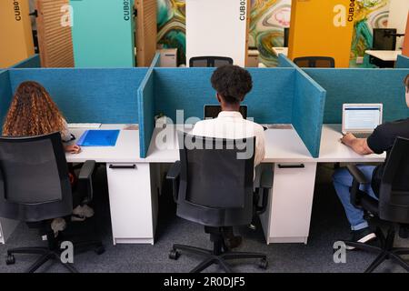 Three young people share coworking space, work side by side with desk ...