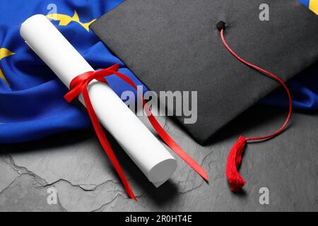 Black graduation cap, diploma and flag of European Union on light grey ...
