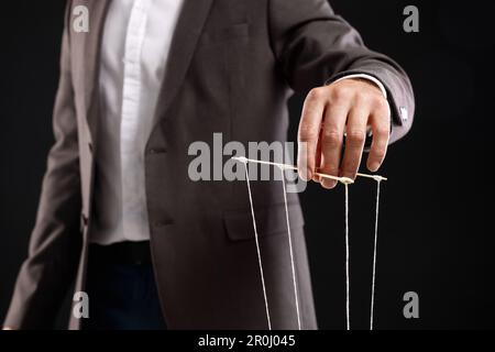 Man in suit pulling strings of puppet on black background, low angle ...