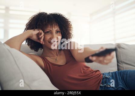 Whats on TV. a young woman watching TV while relaxing on her sofa at ...