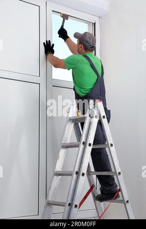 Worker on folding ladder installing window indoors Stock Photo - Alamy