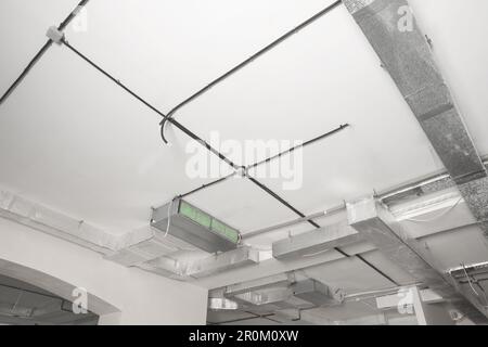 Conduits with cables and ventilation system on white ceiling, low angle ...