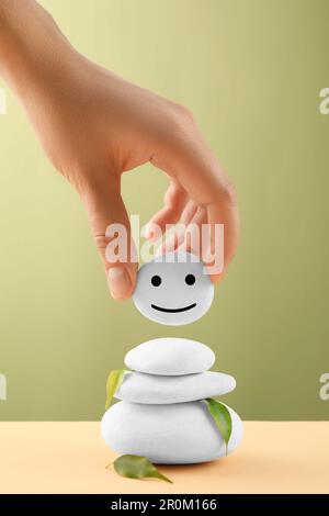 Woman putting stone with drawn happy face on stack against light blue ...