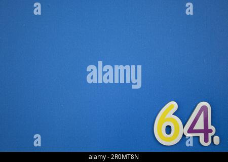 The number 64, placed on a blue background, photographed from above, colored yellow and purple ...