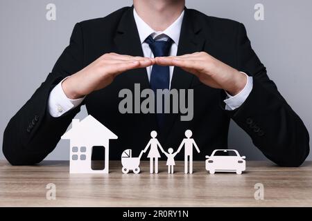 Man protecting figures of family, car and house at wooden table ...