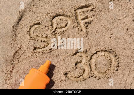 Abbreviation SPF 30 written on sand and blank bottle of sunscreen at ...