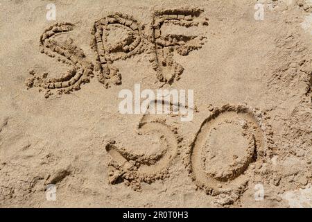 Abbreviation SPF 50 written on sand and blank bottle of sunscreen at ...