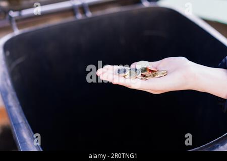 A kid girl hand throws a euro coins into a trash can dumpster, street ...