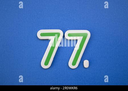 The number 77 in green, photographed from above, placed on the edge of ...