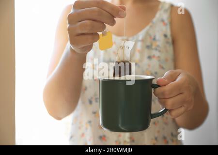 Woman taking tea bag out of cup at table indoors, closeup Stock Photo ...