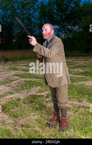An English gentleman stood at twilight in a tweed shooting suit with a ...