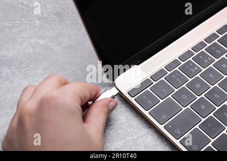 Woman plugging USB cable with type C connector into laptop port at grey ...