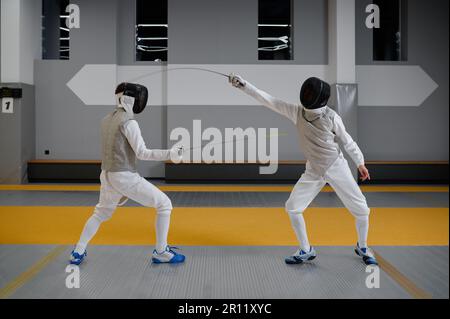Athletes in uniforms and protective helmet mask fighting duel with ...