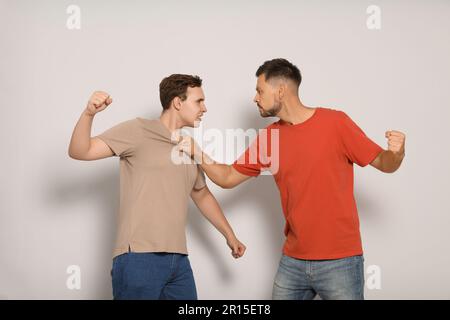 Two emotional men fighting on beige background Stock Photo - Alamy