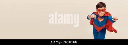 courageous asian boy in superhero costume with cloak and mask standing ...