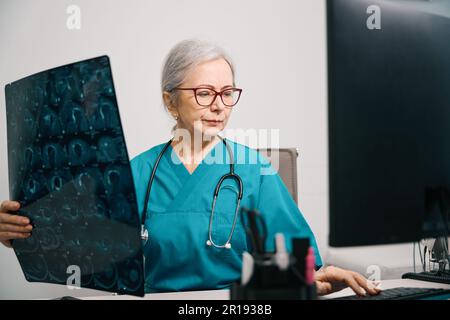 Elderly medical worker holds an MRI scan of the brain in her hands ...
