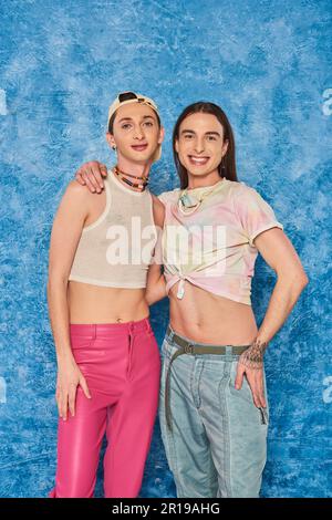 Positive and tattooed gay man hugging friends holding lgbt flags and ...
